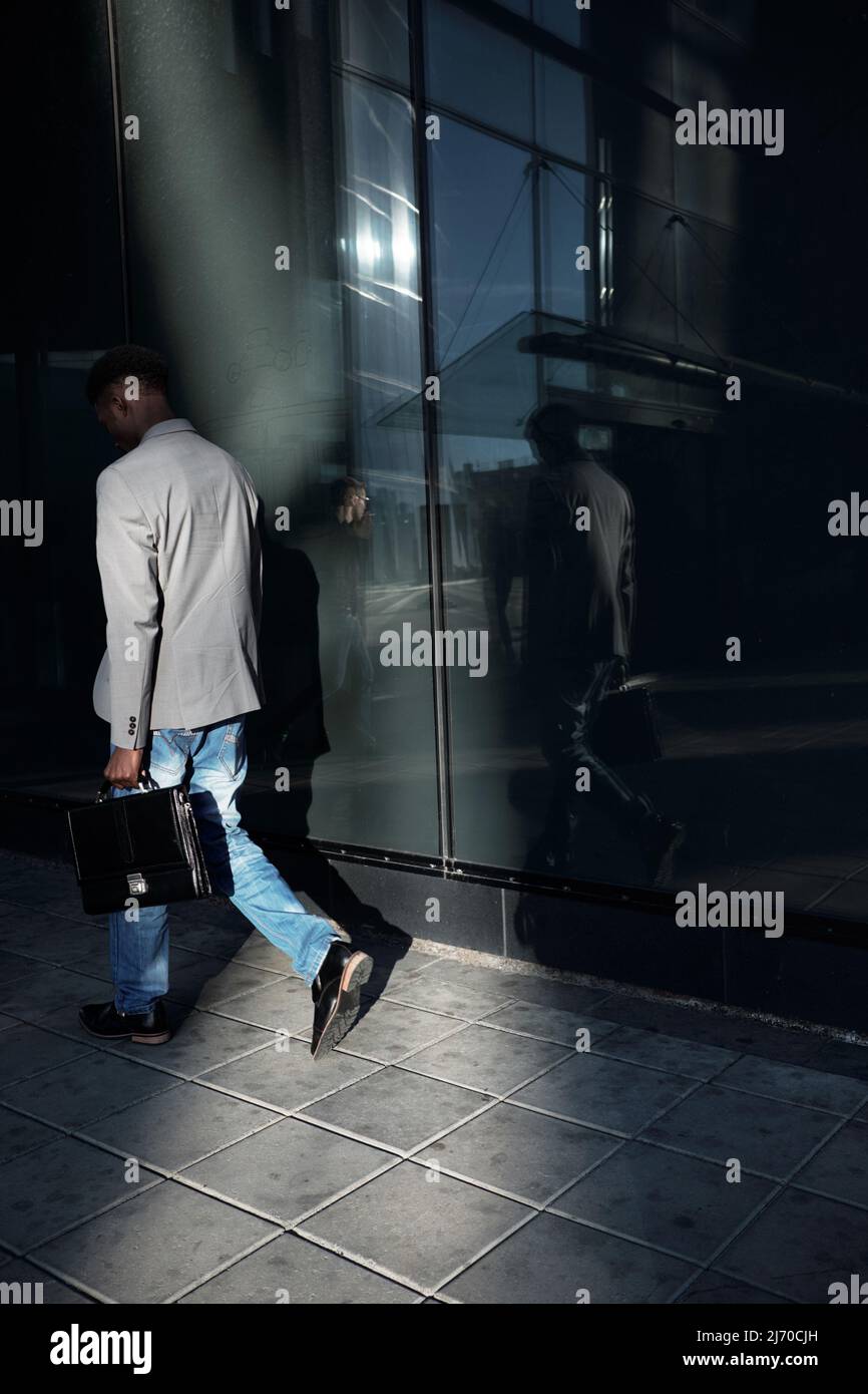 African American office worker with case moving along sidewalk by ...