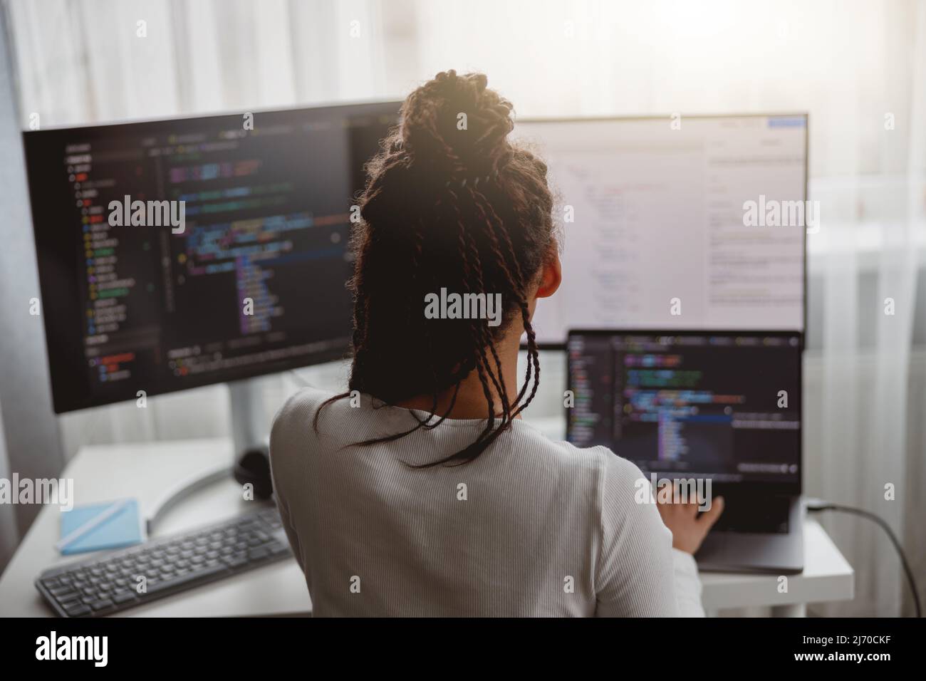 Rear of female web expert typing on computer looking at monitors while ...