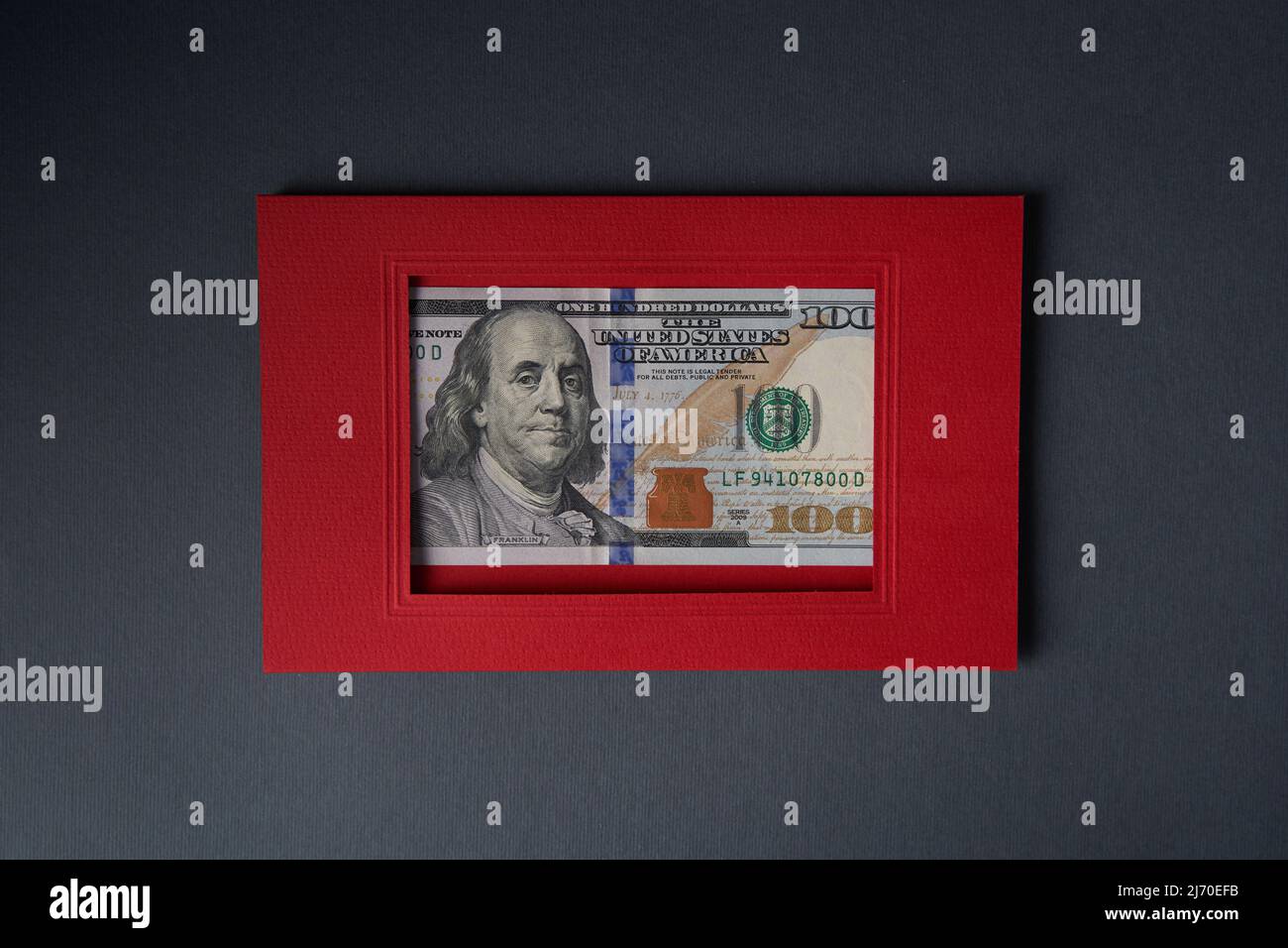 One hundred dollars banknote in a red cardboard frame on a gray ...