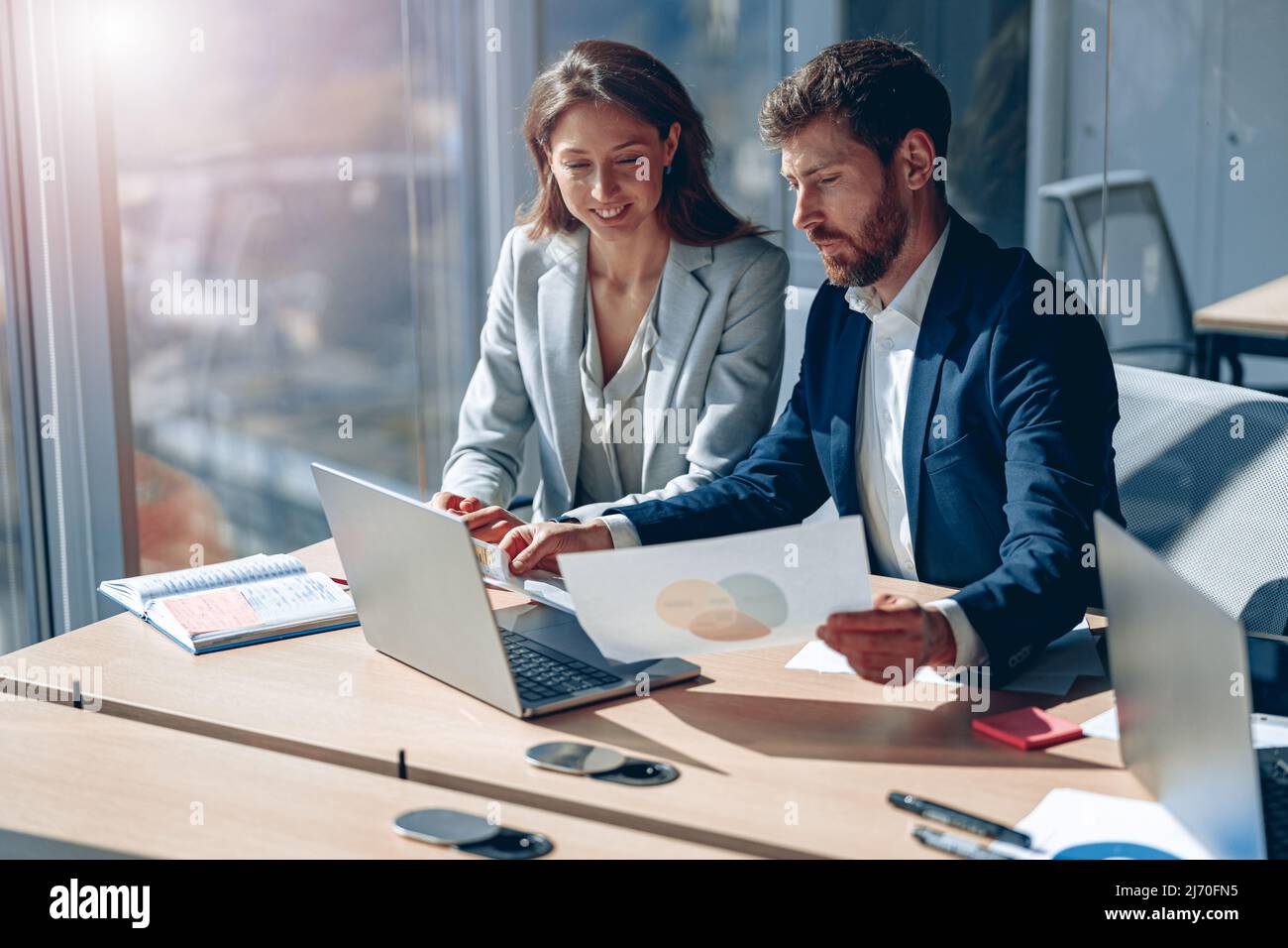 Two smiling business people in modern office explaining statistics data ...