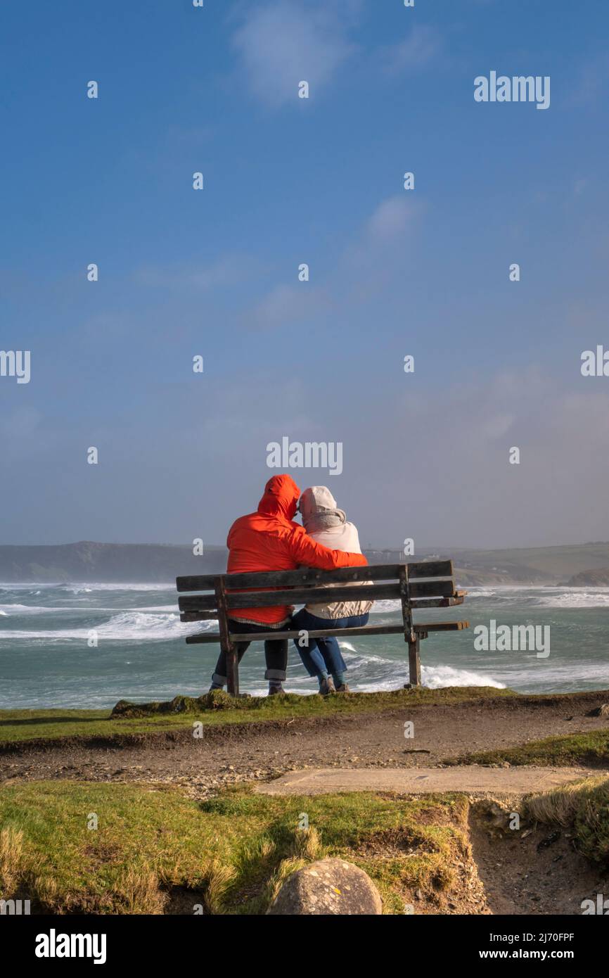 A couple sitting on a bench with their hoods up in high wind brought by ...