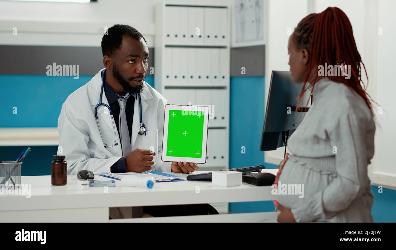 Physician and woman with baby bump looking at greenscreen on digital ...
