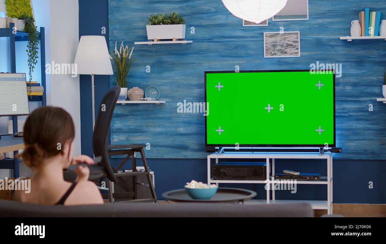 Young woman relaxing televison on green screen mockup display changing stations with remote ...