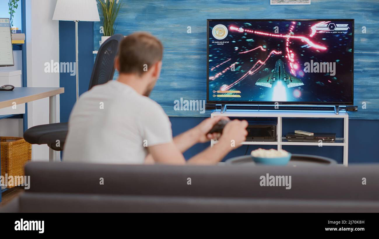 Man holding controller playing action space shooter on console ...