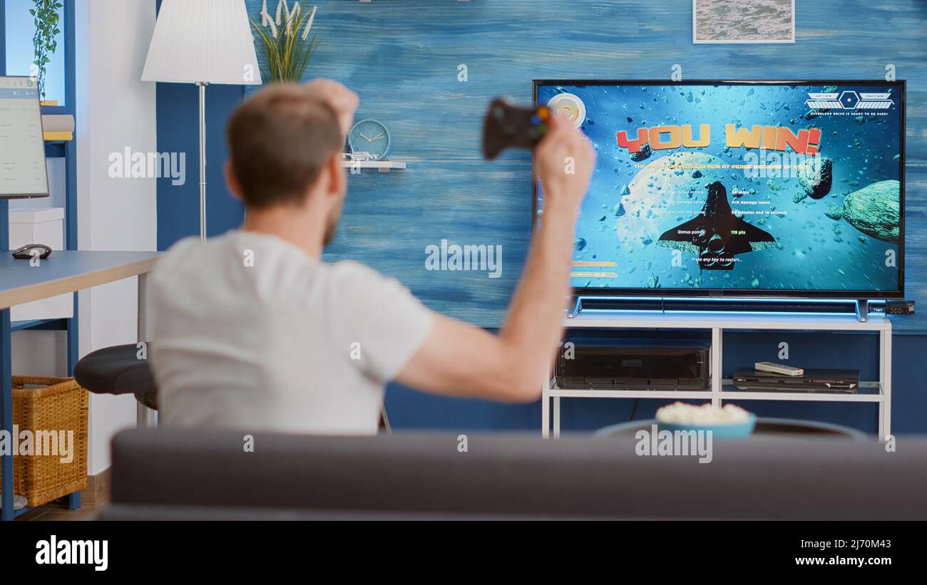 Gamer holding controller celebrating victory in online first person ...