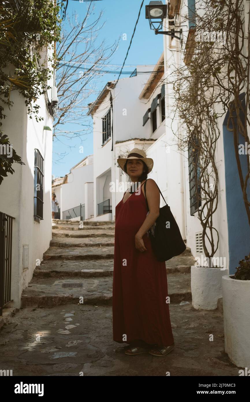 young pregnant woman with red dress and hat walking in traditional ...
