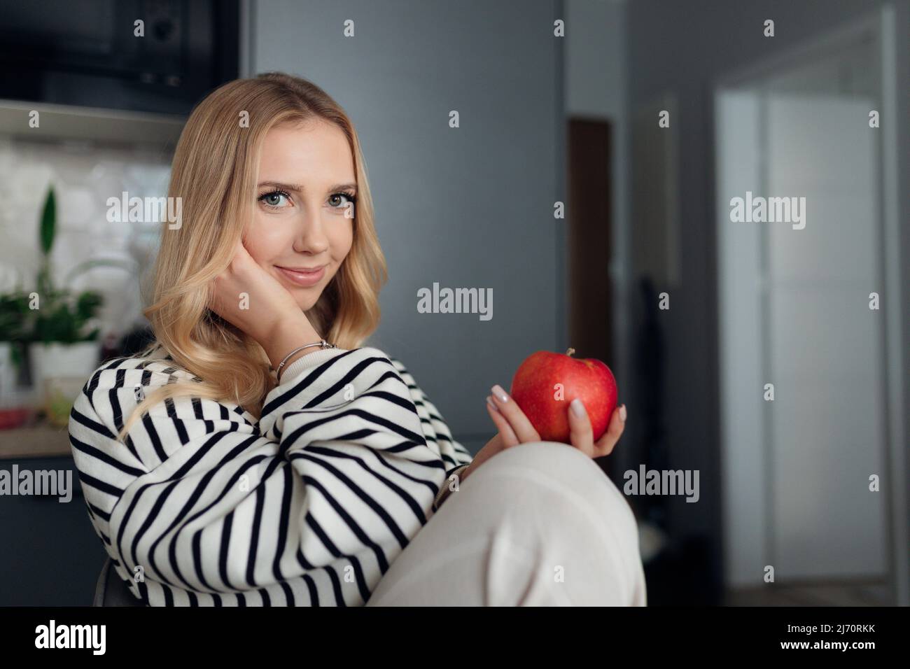 Young happy woman holding red ripe apple and smiling sitting on chair ...