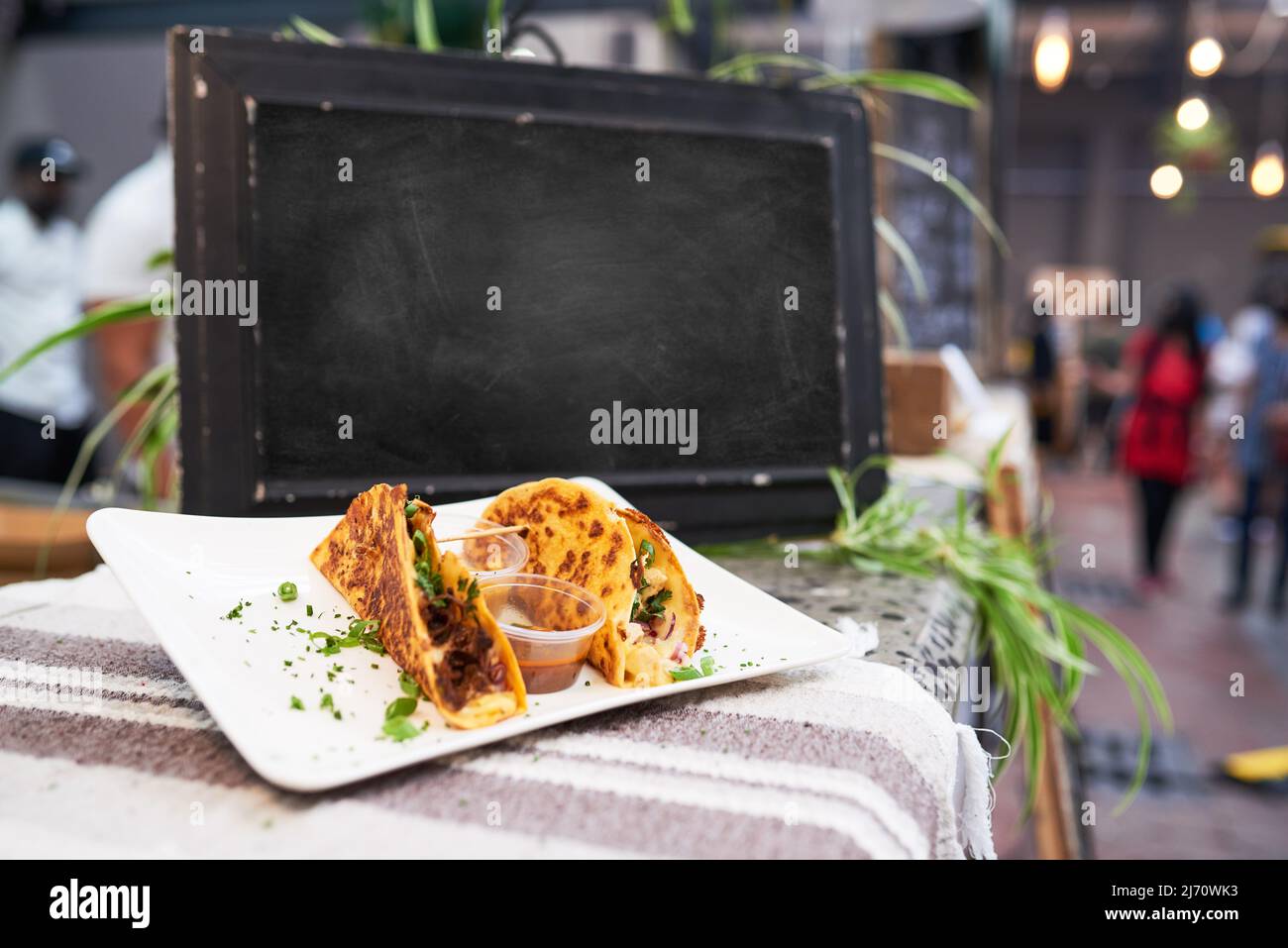 An empty chalkboard at a market with soft shell tacos in foreground ...