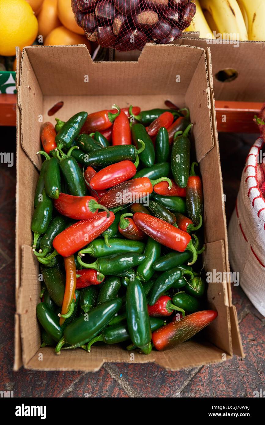 A cardboard box filled with red and green chilis at a vegetable market ...