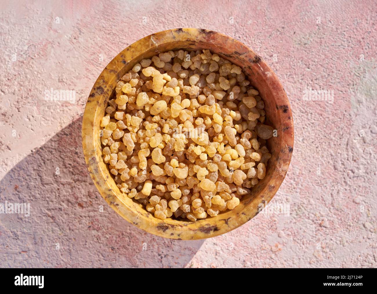 Frankincense resin crystals in a bowl on pink background in sunlight ...