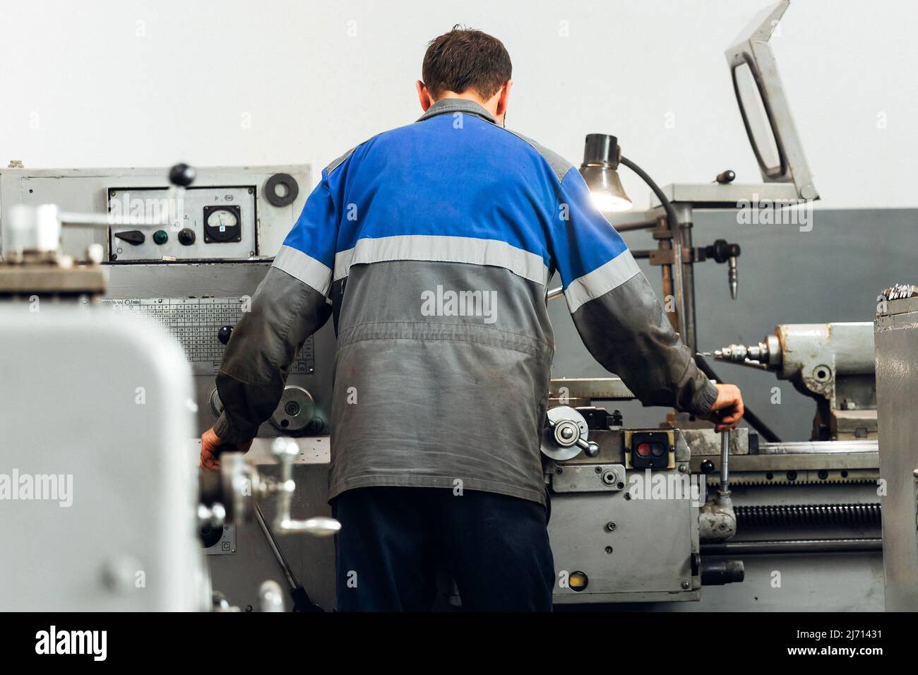 Turner stands behind lathe in production hall and works. View of worker ...