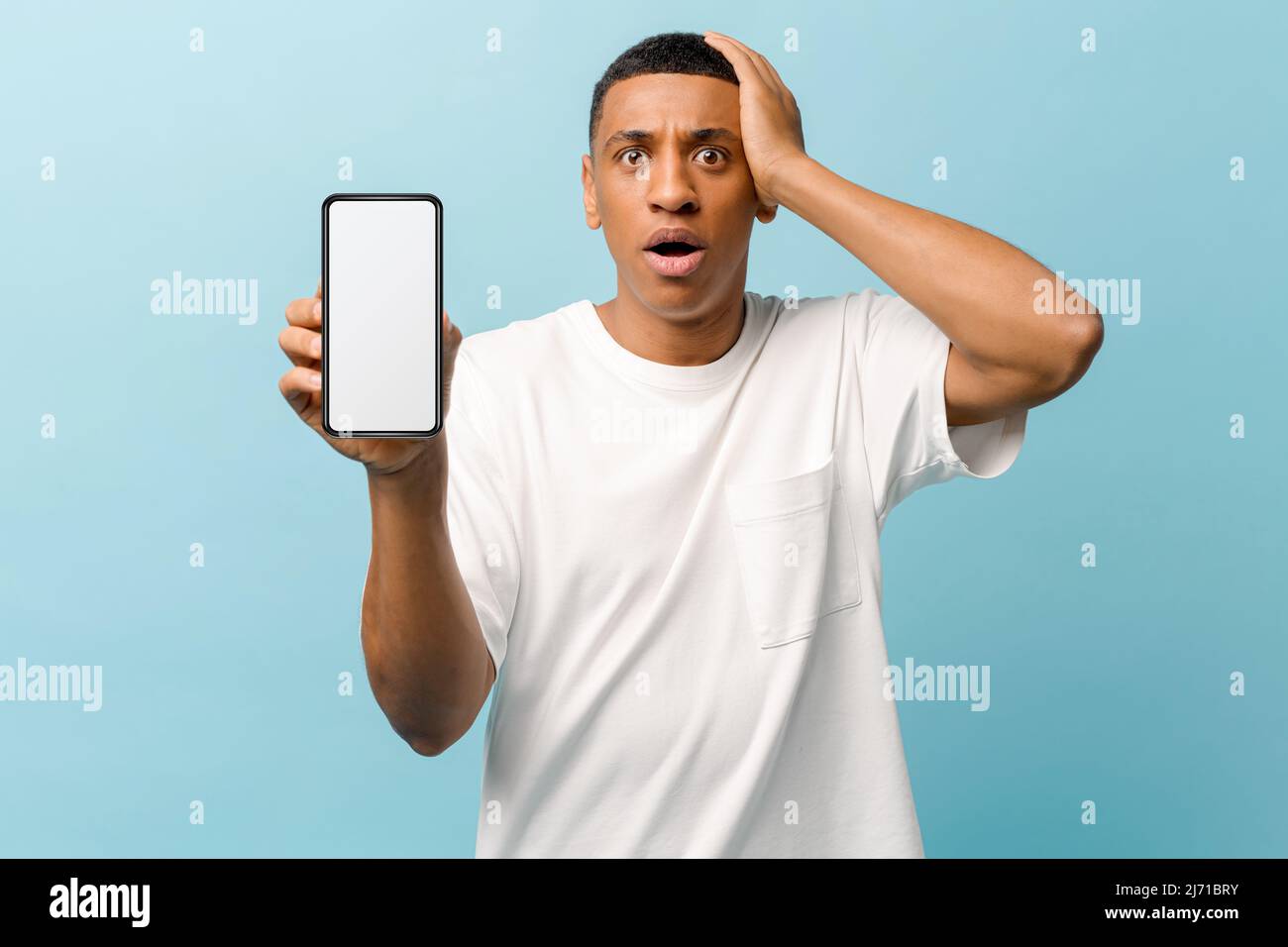 Worried African-American young guy showing smartphone with blank screen ...