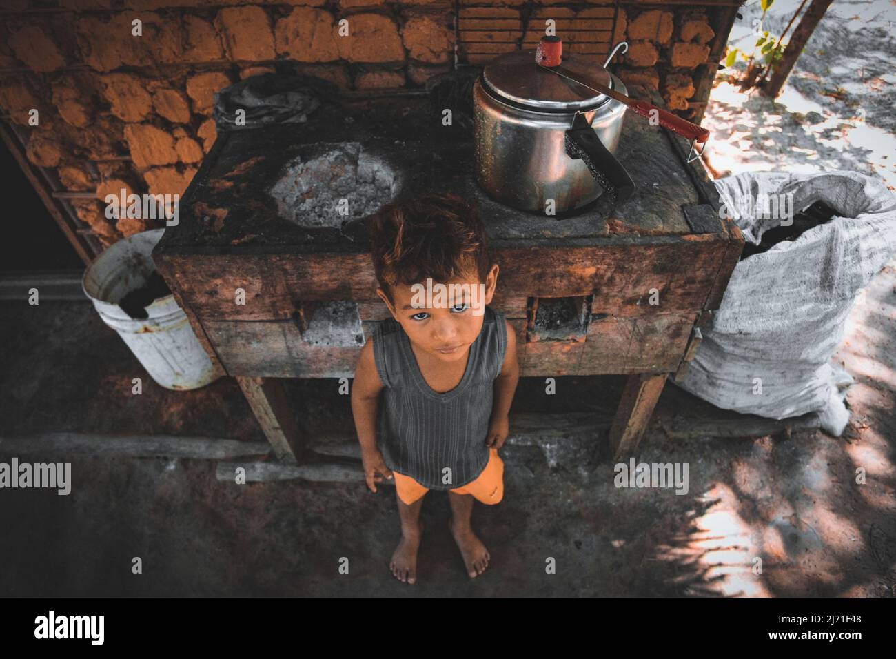 Poverty-stricken child standing in front of a makeshift kitchen outside ...
