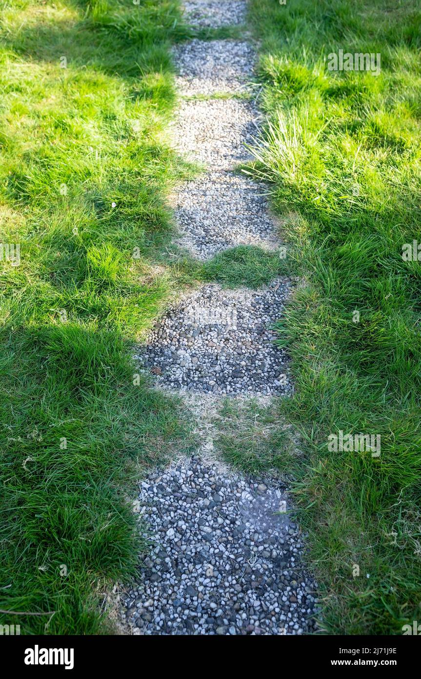 Path made of small stones, a well-groomed lawn with fresh green grass ...