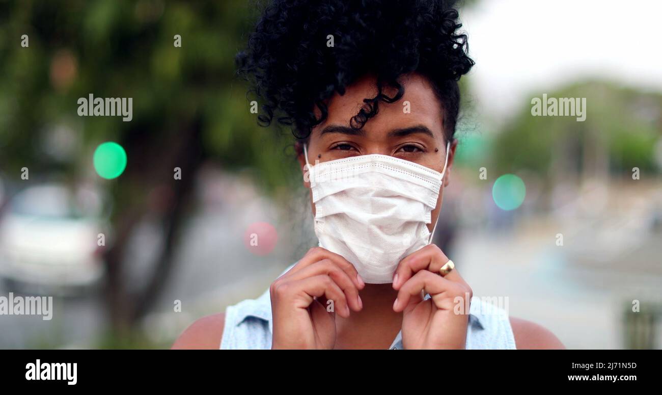 Mixed race woman putting covid-19 face mask outside in urban background ...