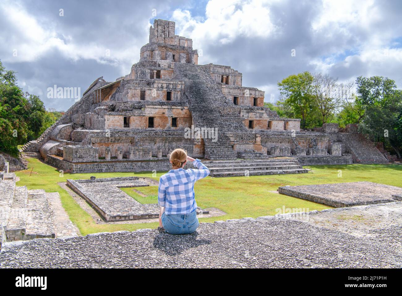 A young tourist woman sitting and looking at mayan ruins of Temple of the Five Storeys, Edzna ...