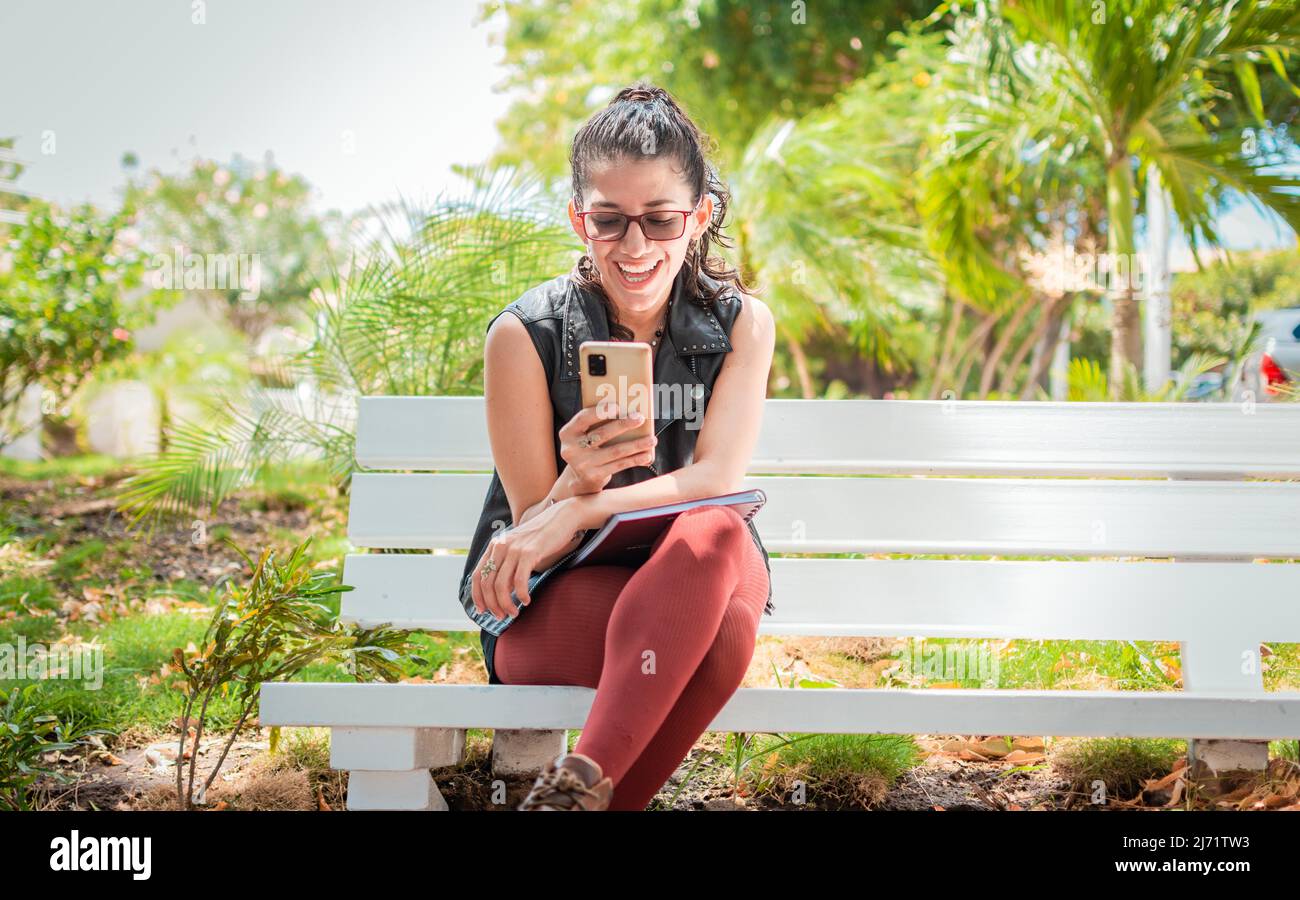Girl sitting on a bench checking her cell phone, Happy woman sitting in a park texting on her ...