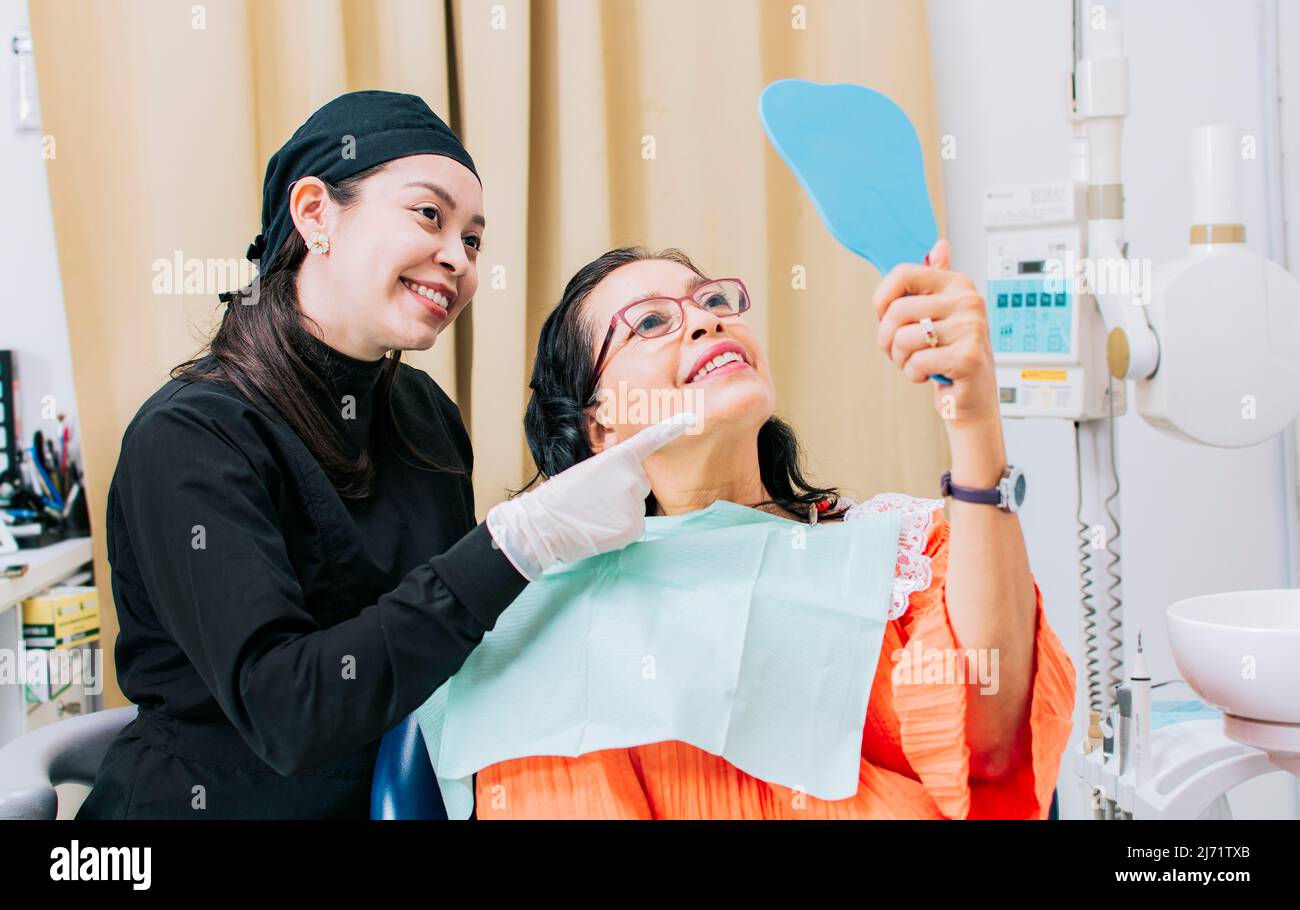 Satisfied female client in dental clinic looking at mirror, Dentist with patient smiling at hand ...
