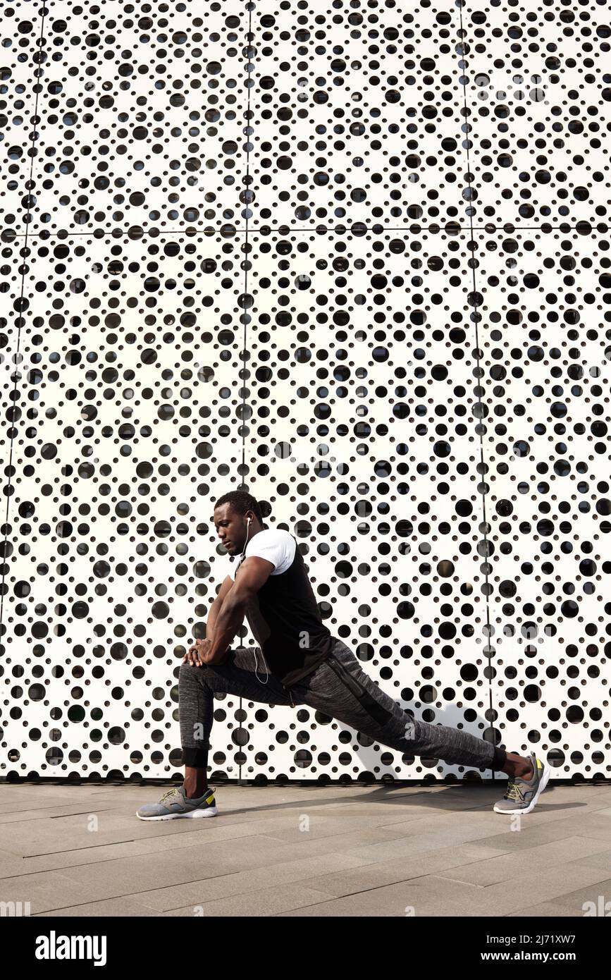 Young athletic African American man doing stretching exercise outdoors ...