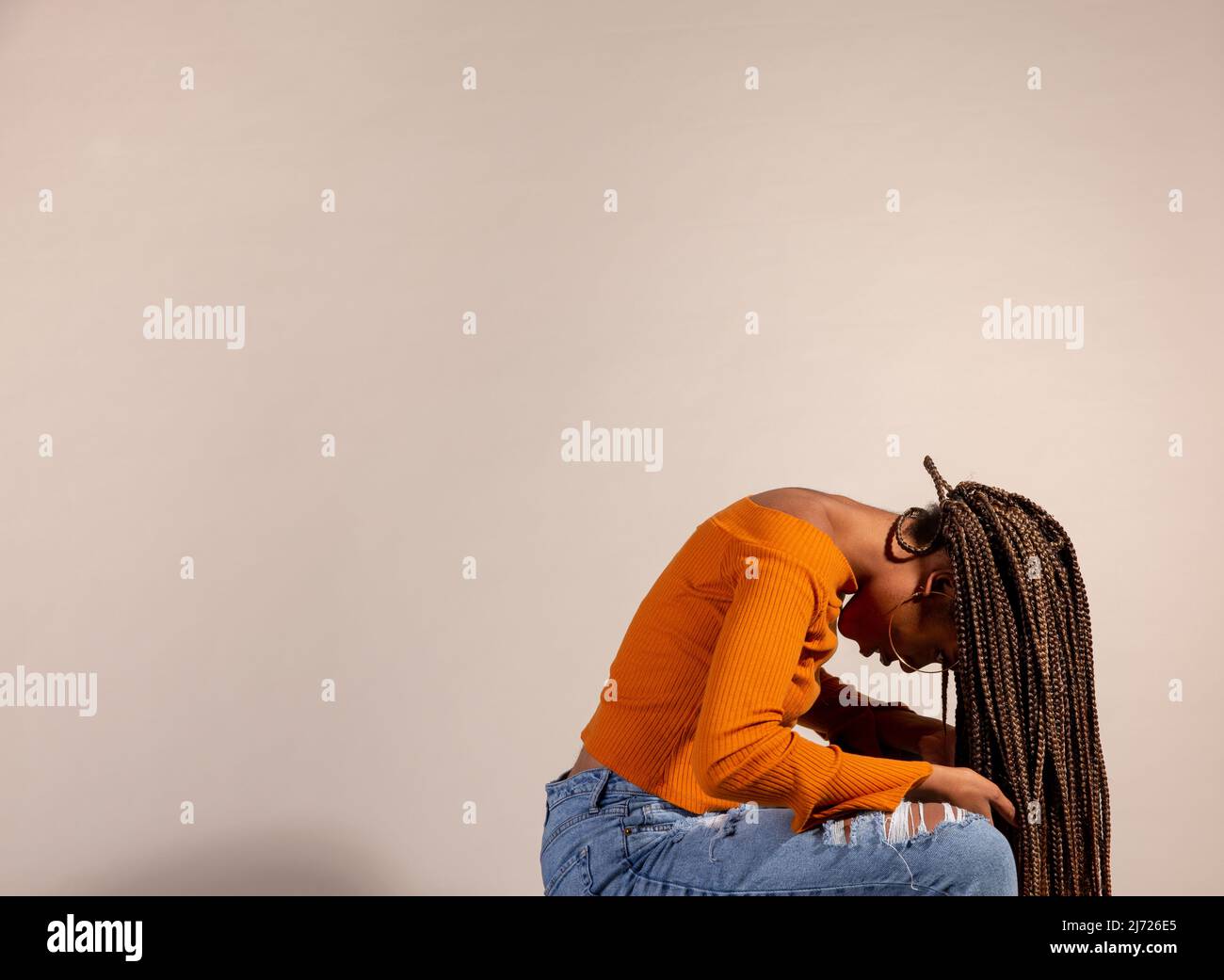 Studio shot of a young Black woman looking down with hair over her face ...