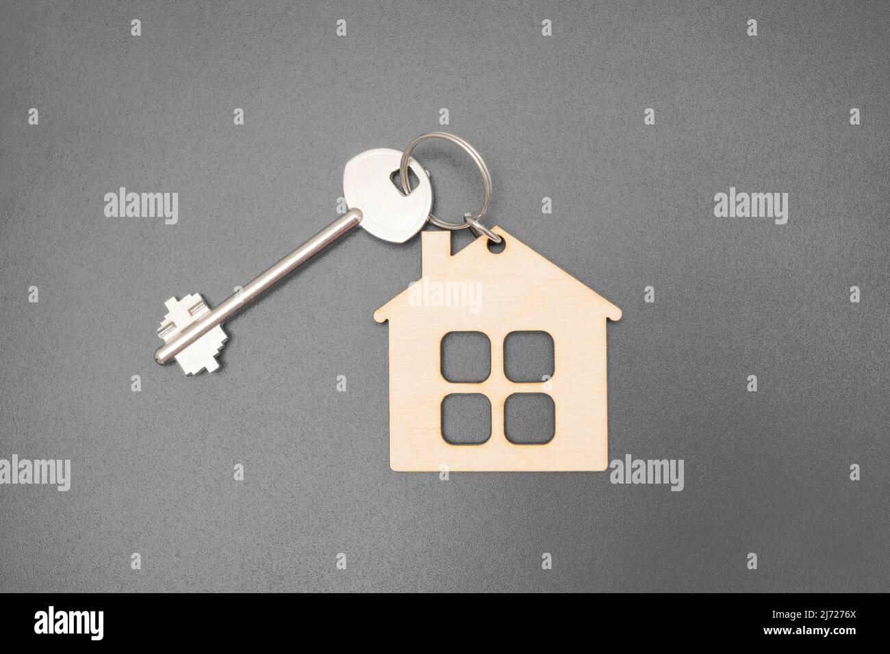 Flat wooden house shaped key chain with a key isolated on a gray ...