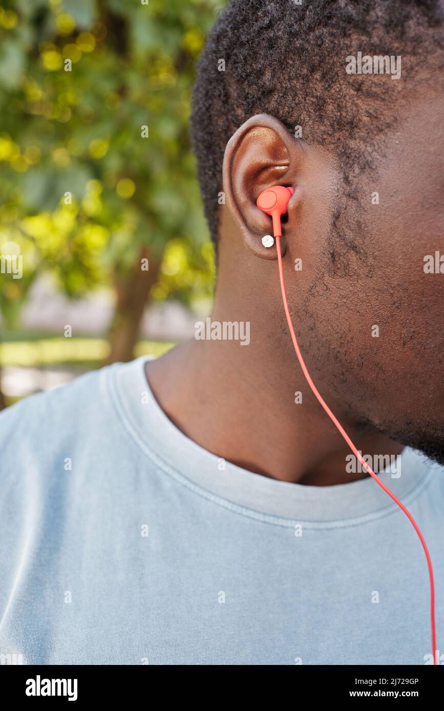Unrecognizable Black guy listening to music through modern red earbuds ...