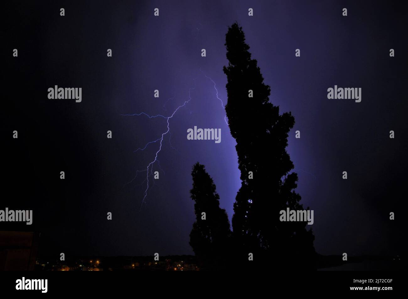 Bright lightning bolt with two pine trees at night, city in background ...