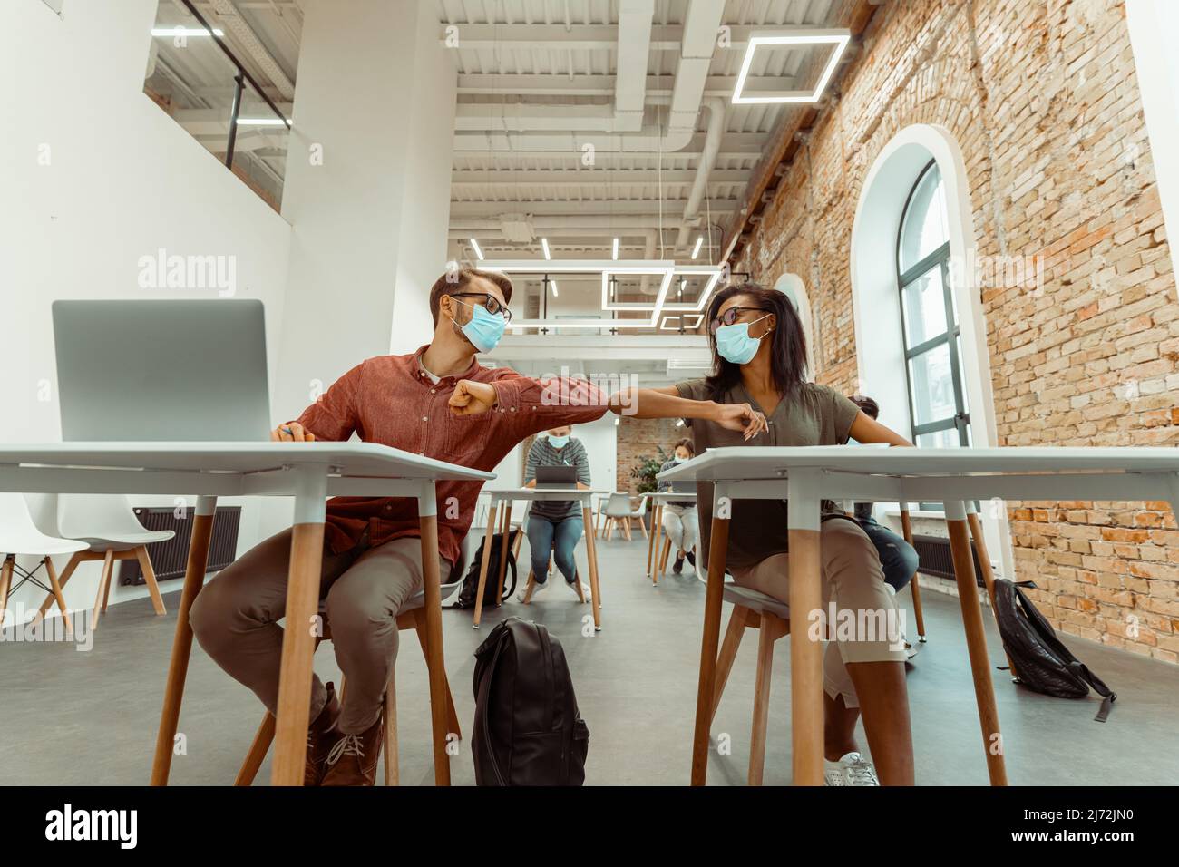 Students siting and greeting bumping elbows at workplace Stock Photo ...