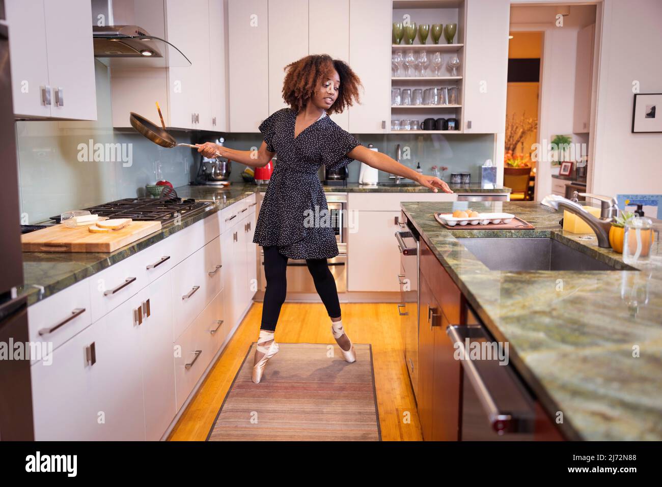 Ballet dancer standing on her toes and reaching for eggs while cooking ...