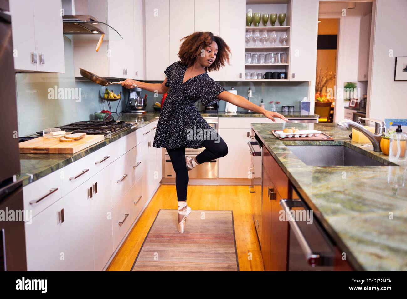 Ballet dancer reaching for eggs while cooking breakfast in kitchen ...