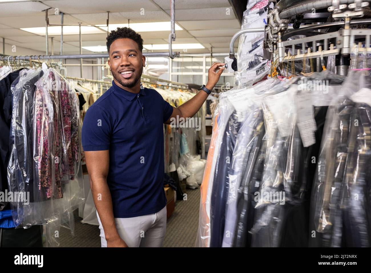 African American man working at dry cleaners pulling clothes off rack ...