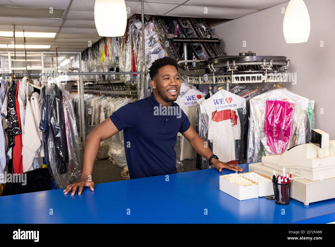 Man behind counter at dry cleaners, talking to customer Stock Photo - Alamy