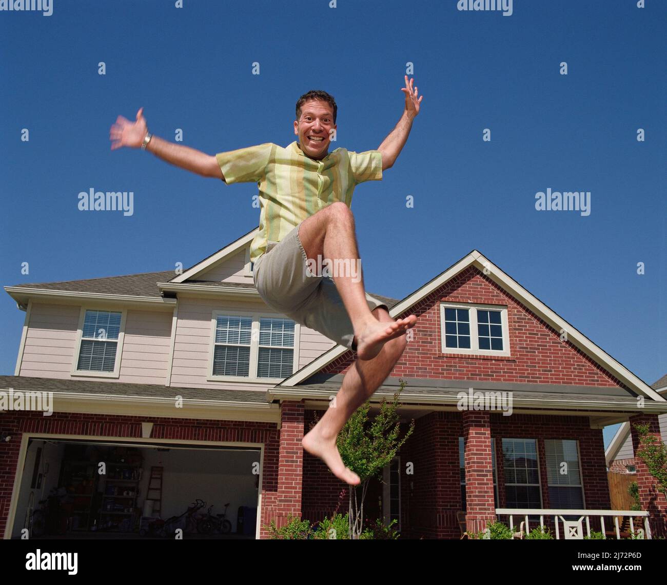 Middle aged man jumping in front of home, striking a pose mid air Stock ...