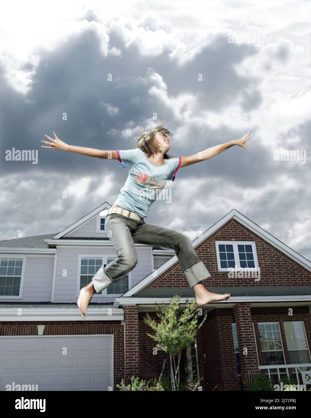 Teenage girl jumping in front of home, striking a pose mid air with ...