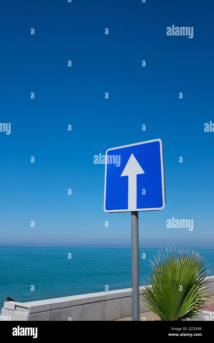 Square road sign with white arrow on blue sky background. It indicates ...