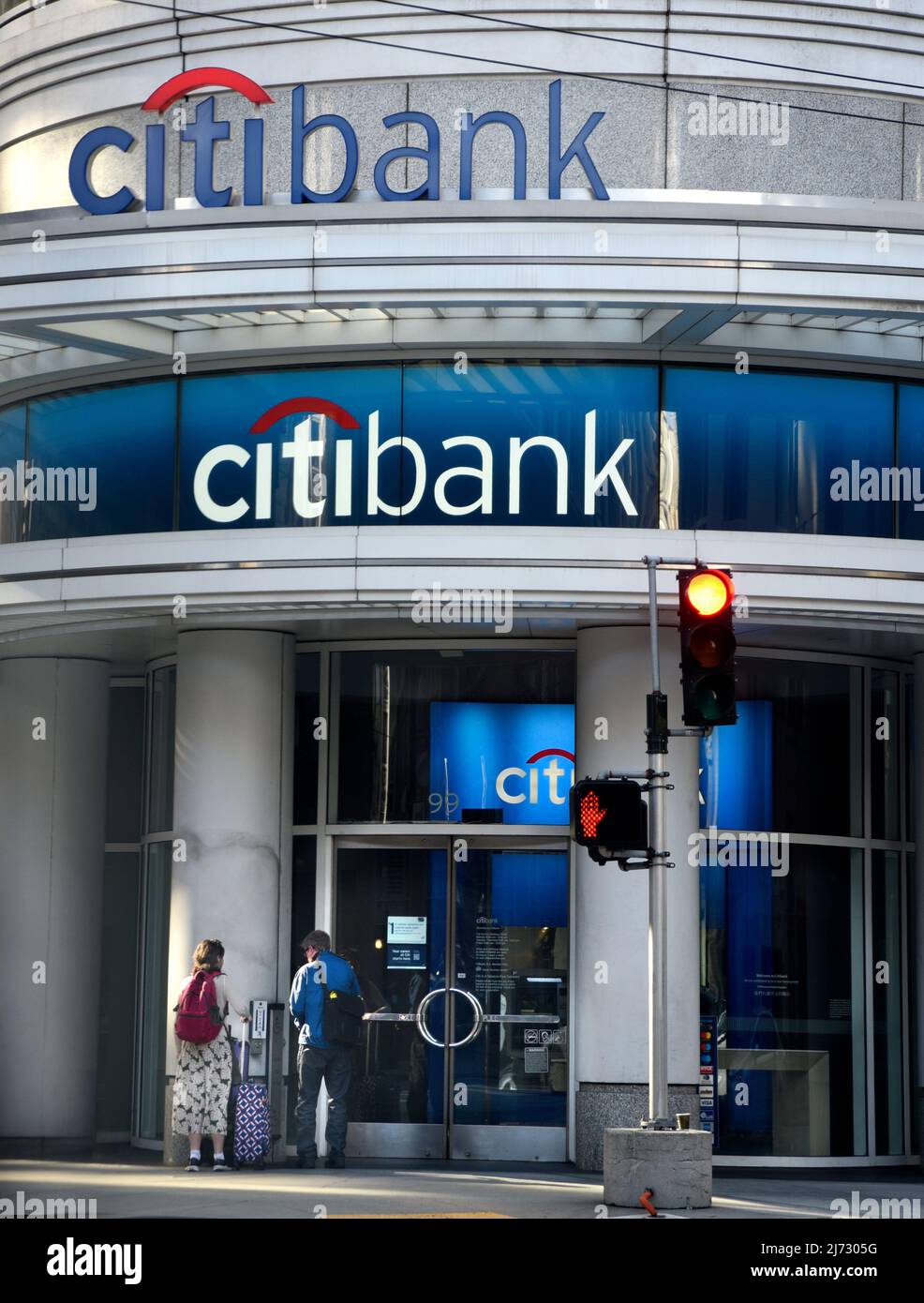 Banking customers, including a couple with suitcases, wait outside for ...