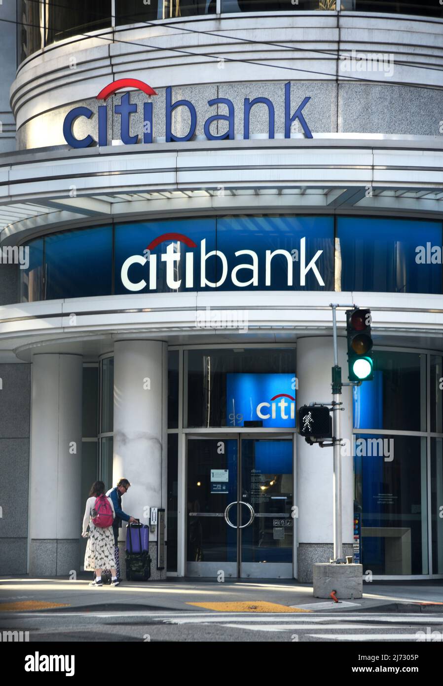 Banking customers, including a couple with suitcases, wait outside for ...