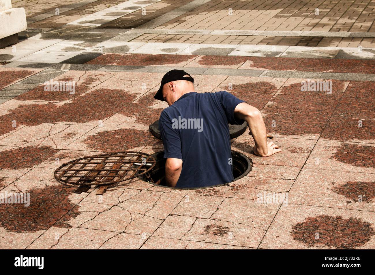 A worker climbs out of an open manhole in the road. Dangerous open ...