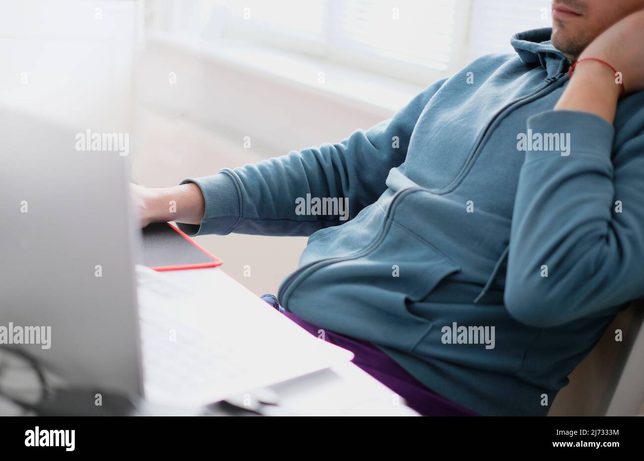 A man in a turquoise sweater in a bright office while working at a ...