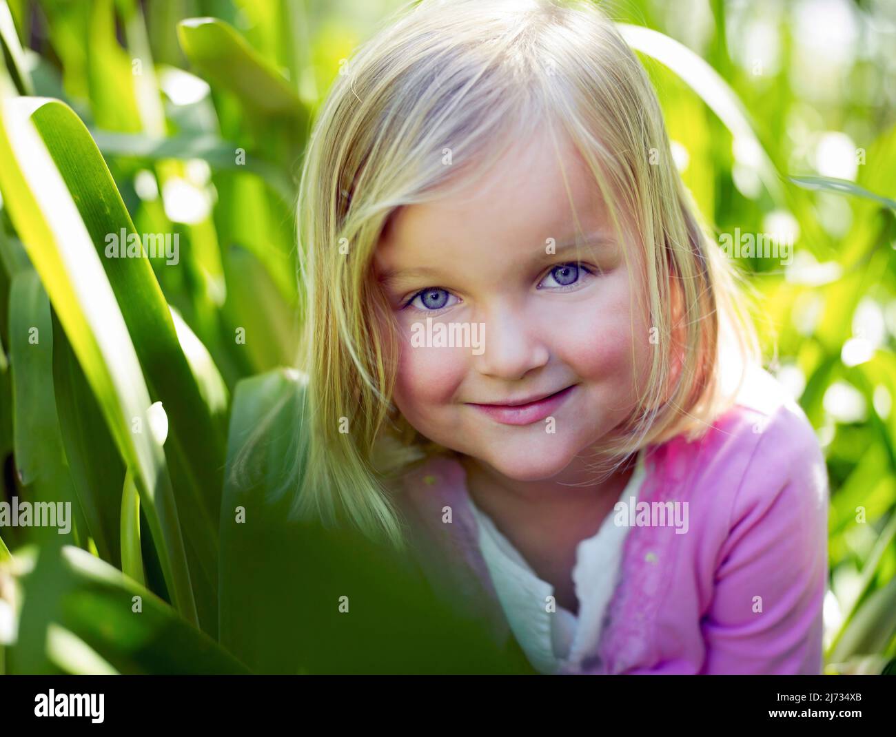 Young blond girl crouching in undergrowth hiding Stock Photo - Alamy