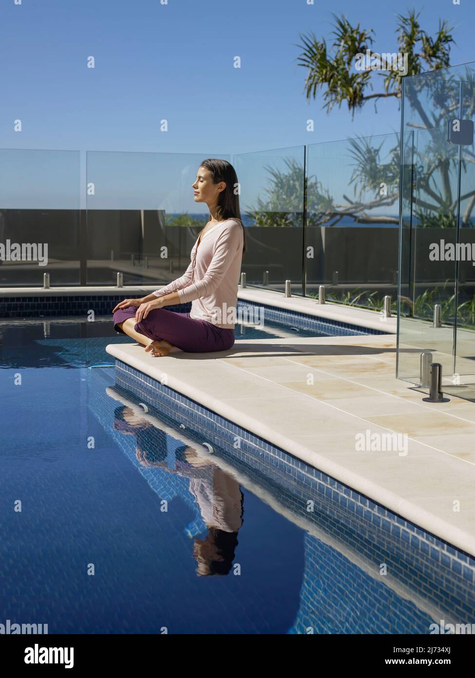 Side view of woman sitting cross legged next to swimming pool ...