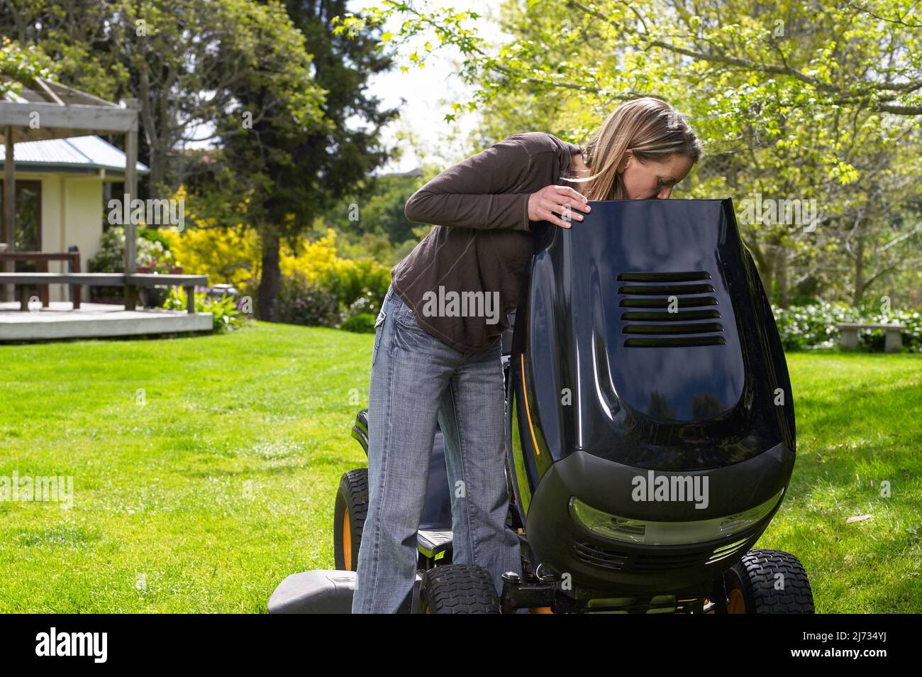 Young woman working under the hood of the ride on lawn mower before ...
