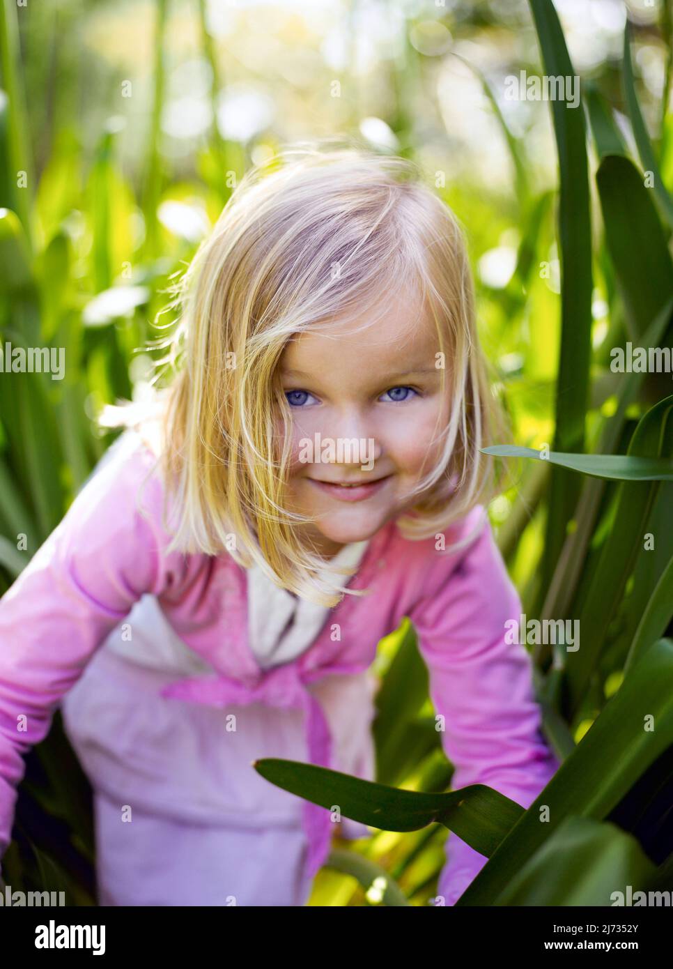 Young blond girl crouching in undergrowth hiding Stock Photo - Alamy