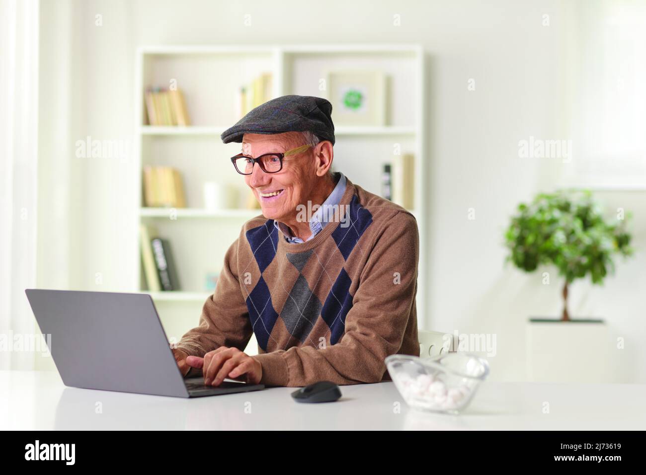 Happy elderly man sitting at home on a sofa with a laptop computer on a ...