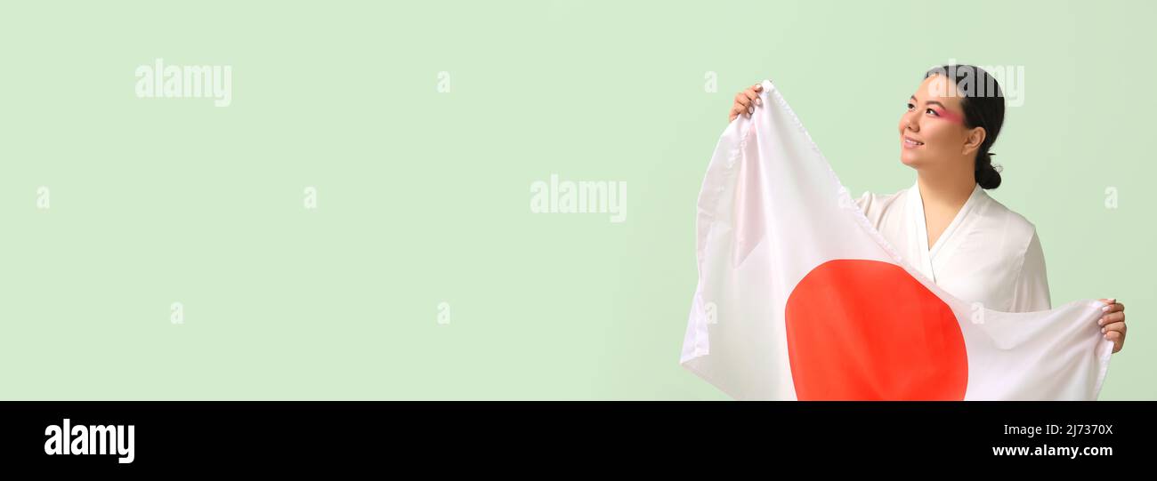 Beautiful young Asian woman holding flag of Japan on light green ...