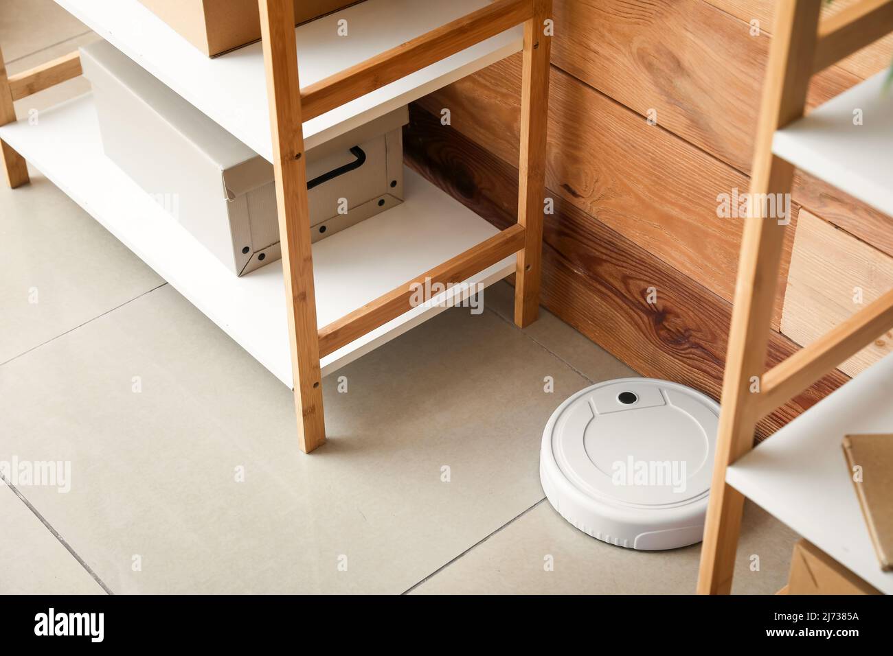 Modern robot vacuum cleaner and shelving units near wooden wall Stock Photo - Alamy
