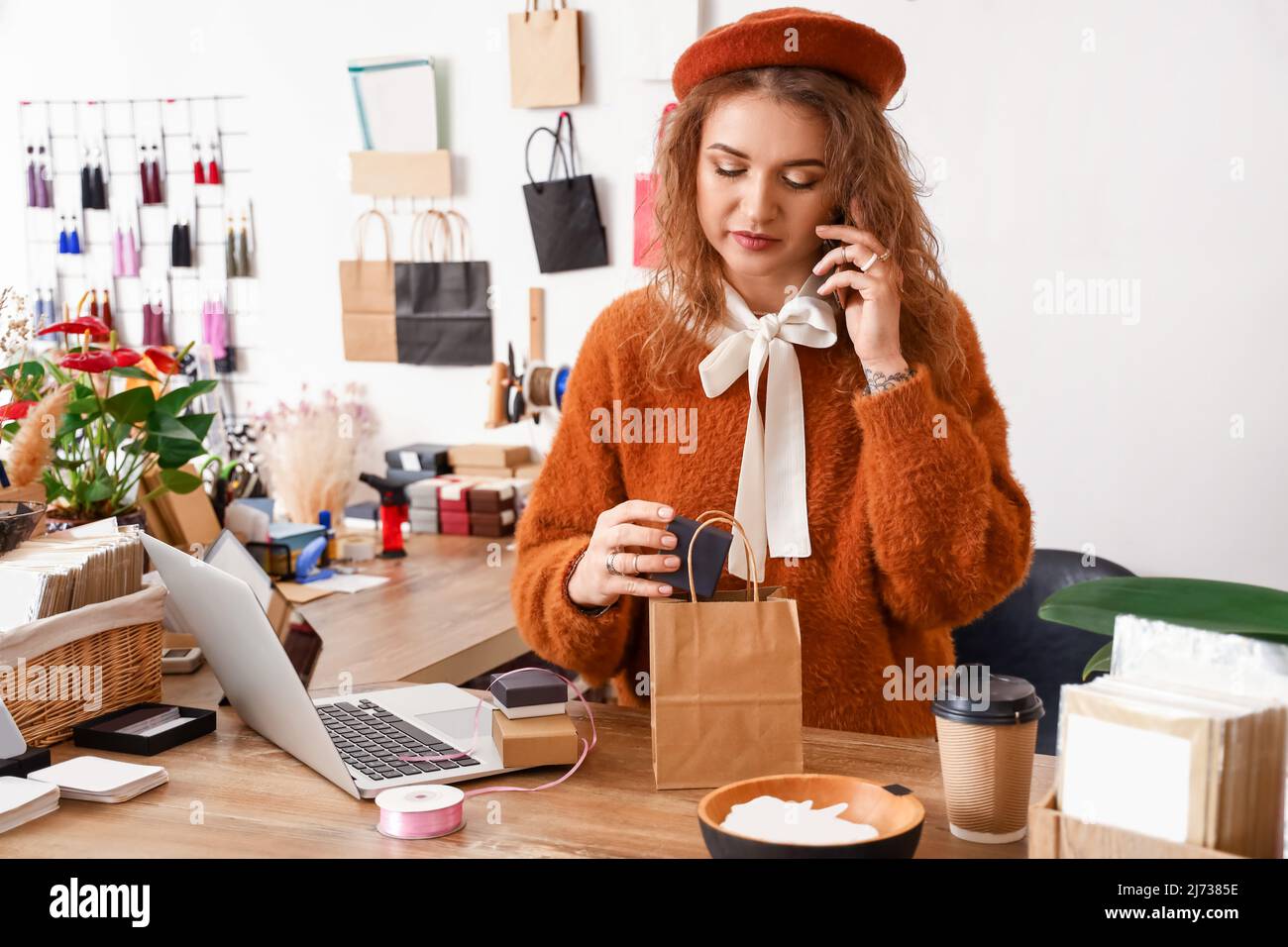 Female business owner talking by phone while packing order in shop ...