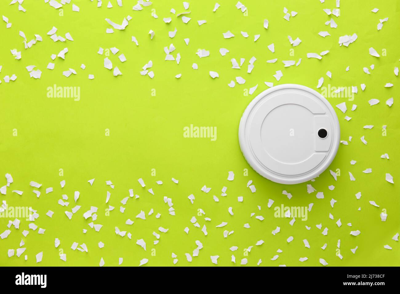 Modern robot vacuum cleaner and torn paper pieces on green background ...