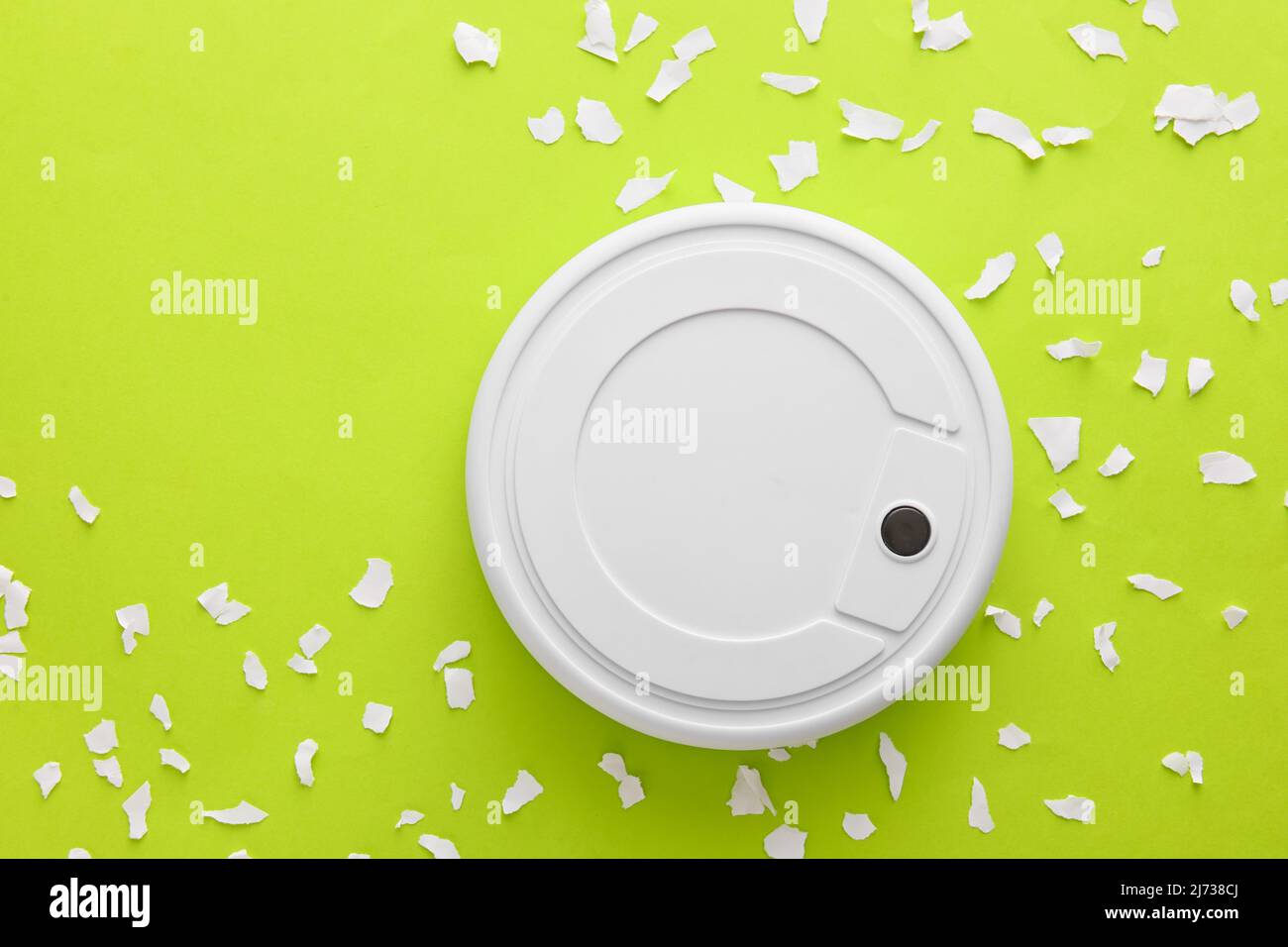 Modern robot vacuum cleaner and torn paper pieces on green background ...