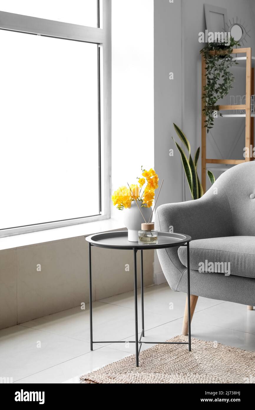 Vase with beautiful flowers and reed diffuser on table near big window ...